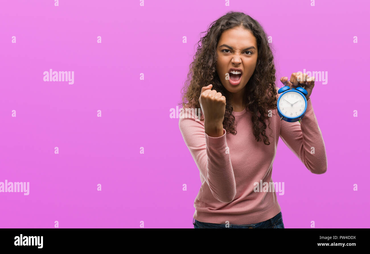 Young hispanic woman holding alarm clock annoyed and frustrated ...