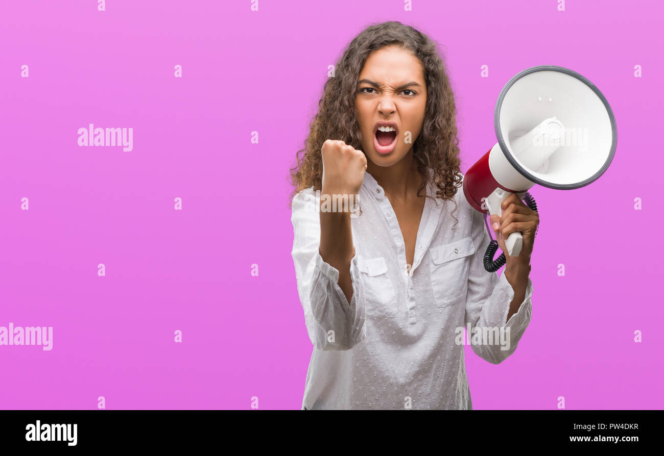 Young hispanic woman holding megaphone annoyed and frustrated shouting ...