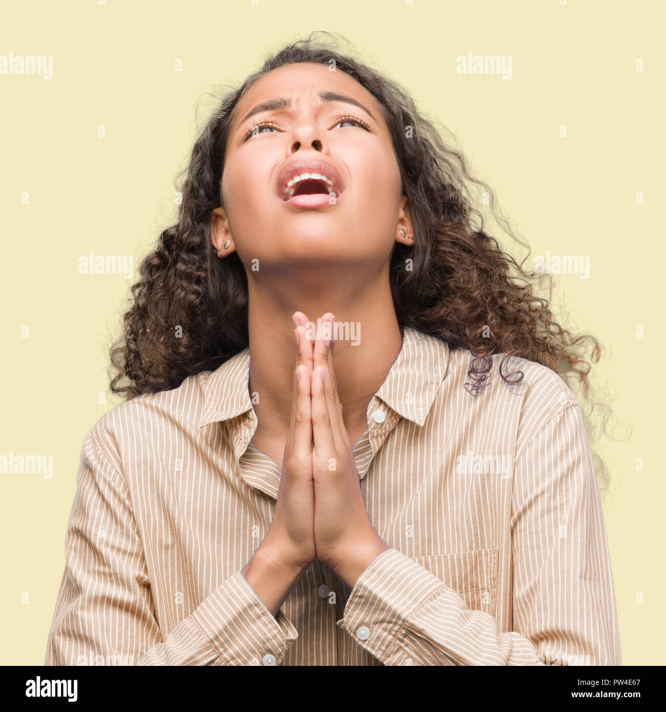 Young hispanic business woman begging and praying with hands together ...