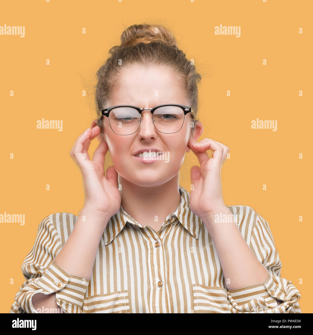 Young blonde business woman covering ears with fingers with annoyed ...