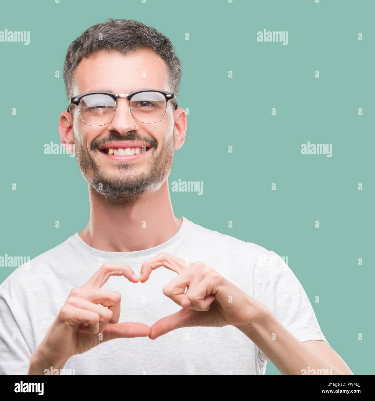 Young tattooed adult man smiling in love showing heart symbol and shape ...
