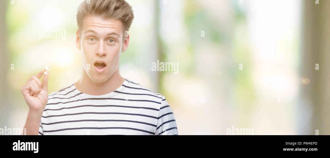 Young handsome blond man eating popcorn scared in shock with a surprise ...