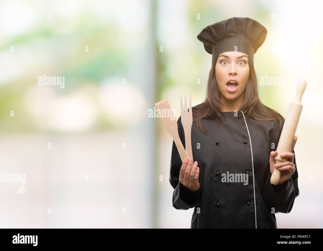 Young hispanic cook woman wearing chef uniform scared in shock with a ...