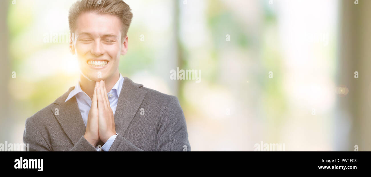 Young handsome blond business man begging and praying with hands ...