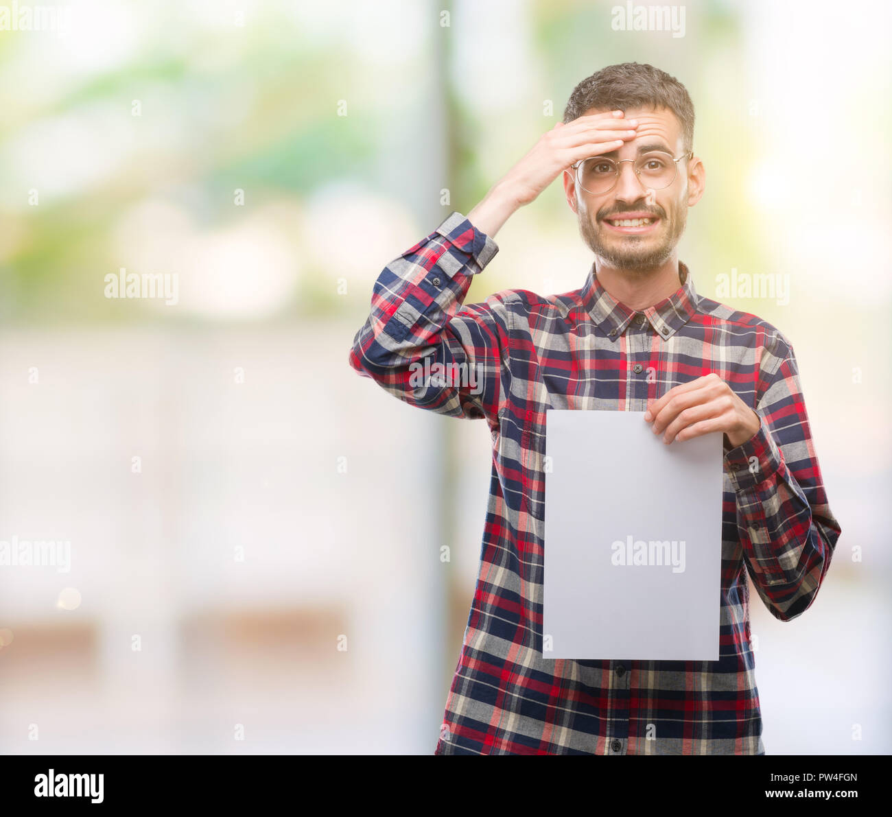 Young hipster adult man holding blank paper sheet stressed with hand on ...