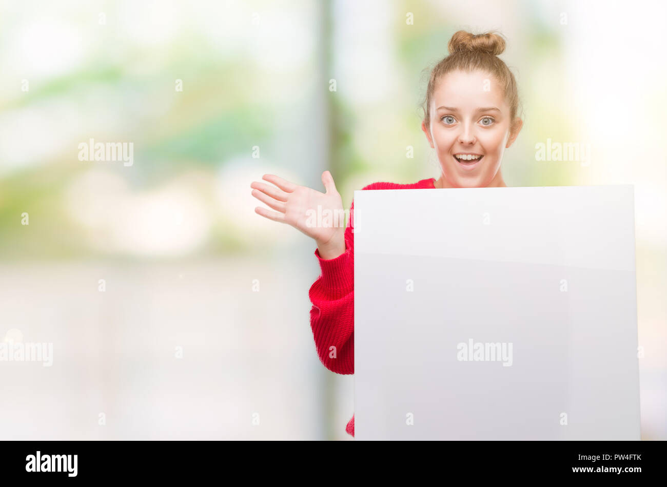 Young blonde woman holding advertising banner very happy and excited ...