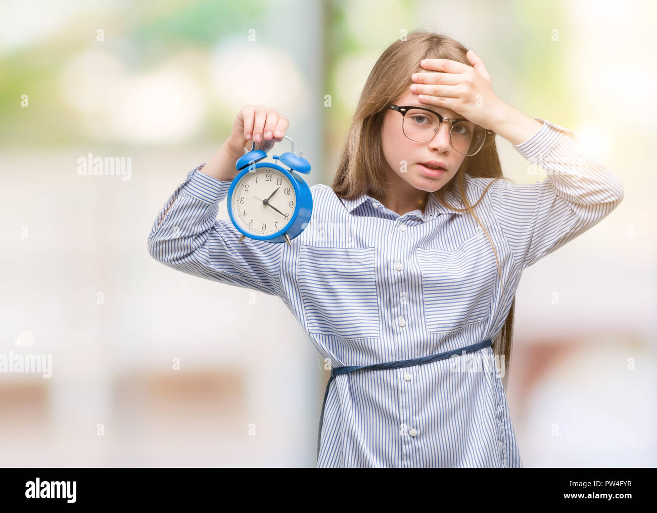 Young blonde child holding alarm clock stressed with hand on head ...