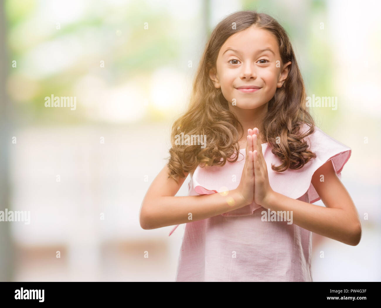 Brunette hispanic girl wearing pink dress praying with hands together ...