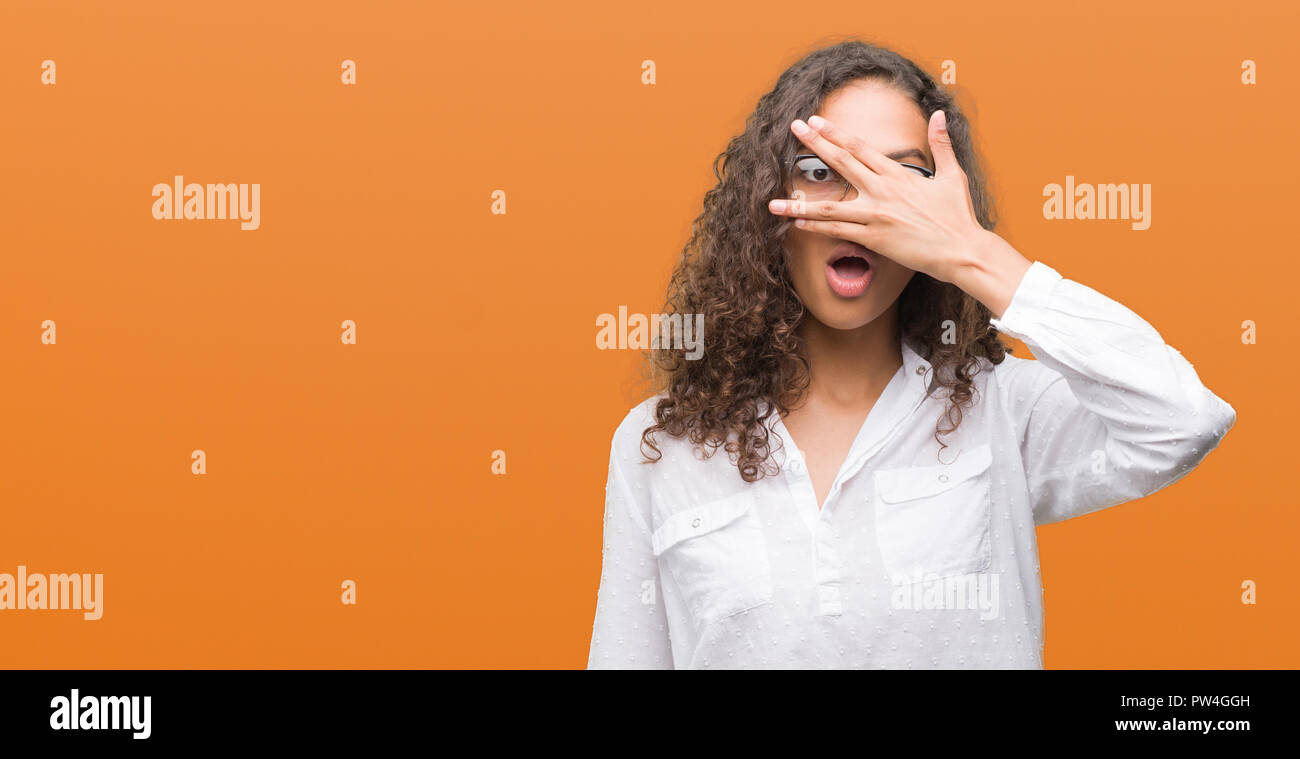 Beautiful young hispanic woman peeking in shock covering face and eyes ...