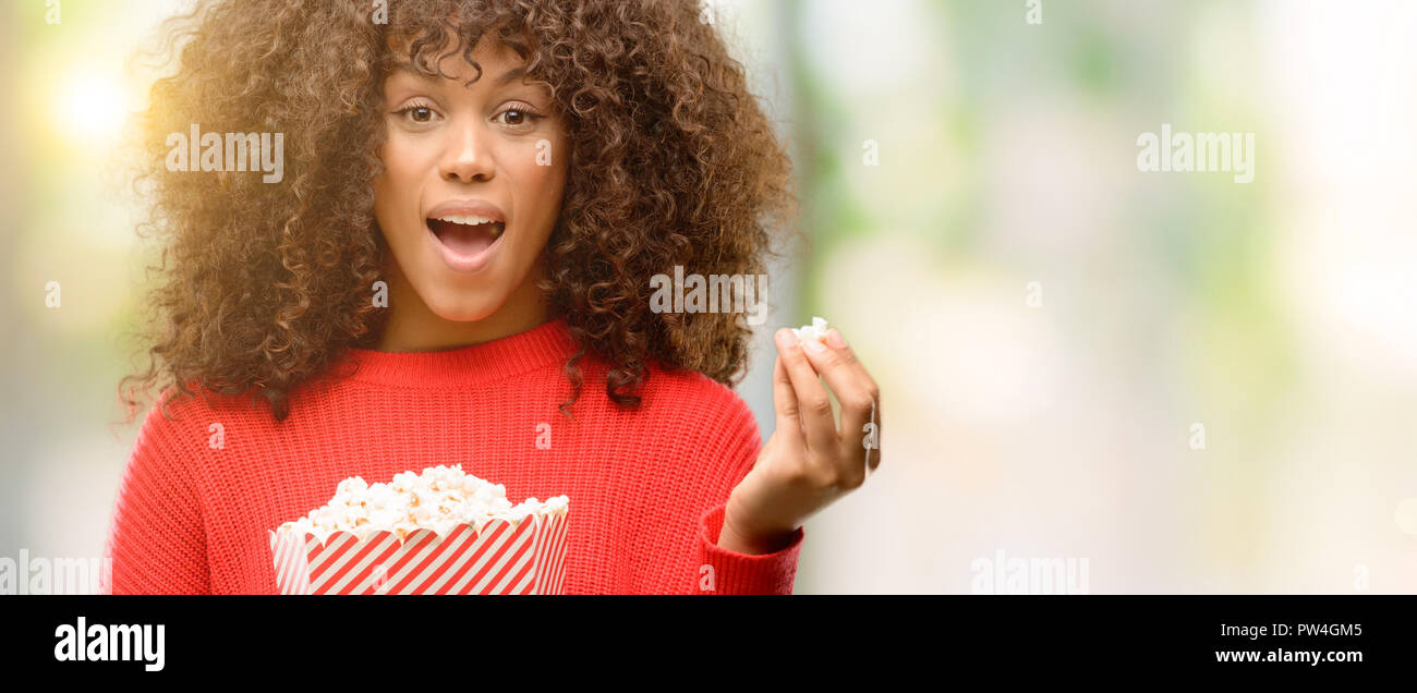 African american woman eating popcorn scared in shock with a surprise ...