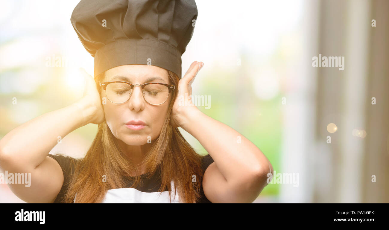 Middle age cook woman wearing chef apron covering ears ignoring ...