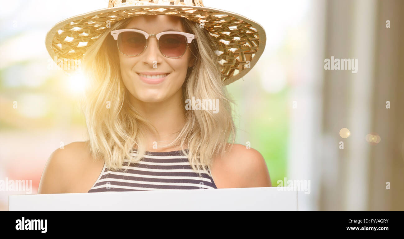 Young woman using sunglasses wearing summer hat holding blank ...