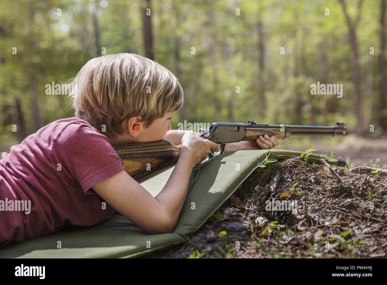 Boy aiming rifle while lying on mat in forest Stock Photo - Alamy