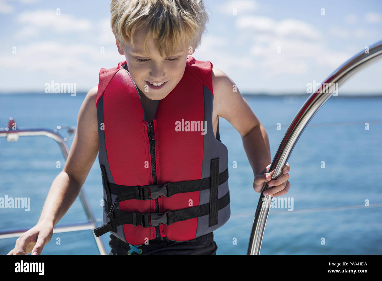 Boy wearing life jacket while standing by railing over sea against sky ...