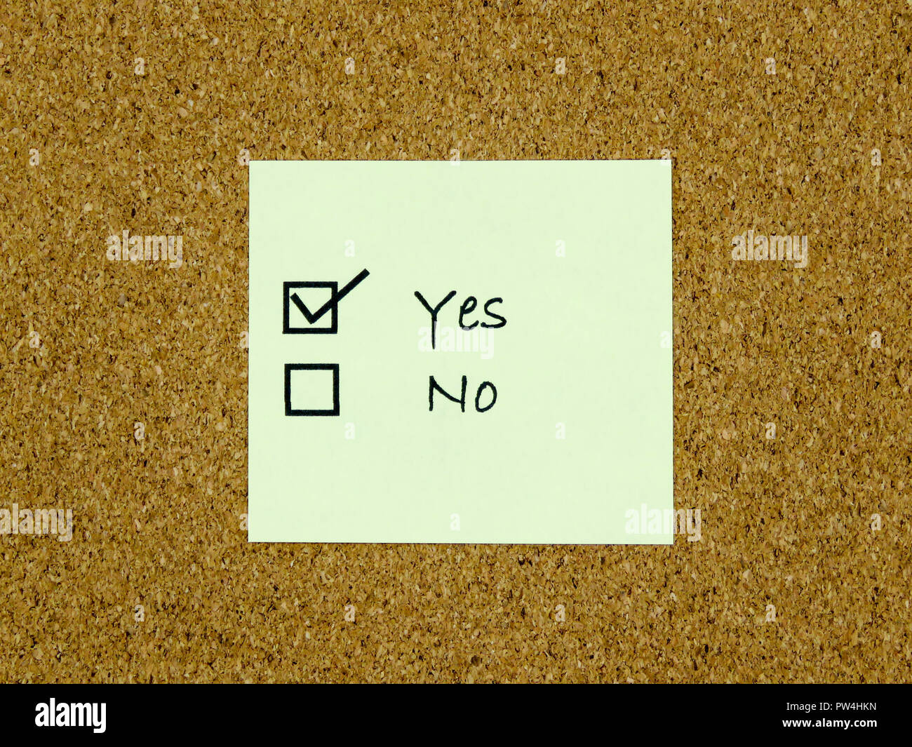 A yellow sticky note with yes / no written on it on a cork board ...