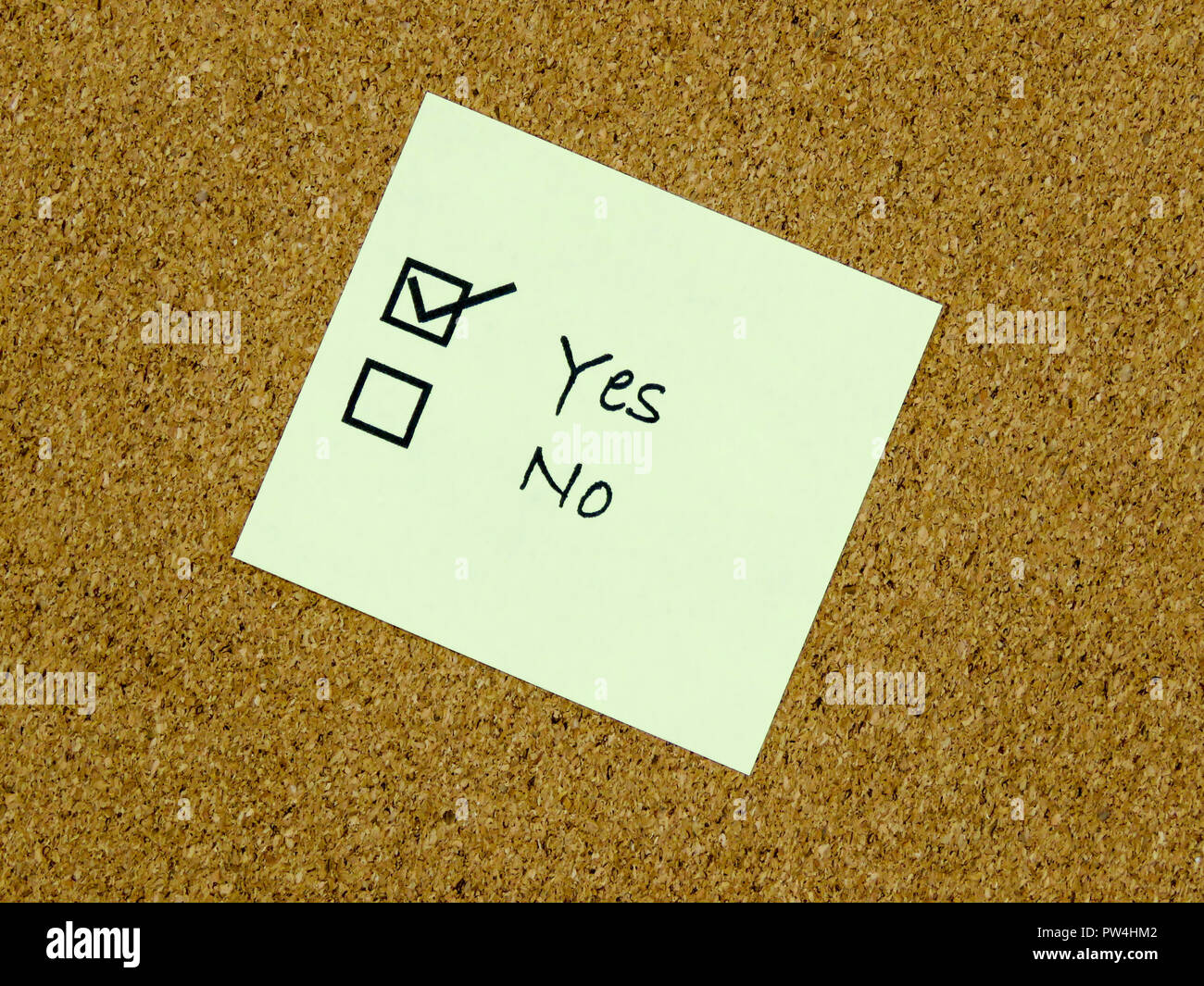 A yellow sticky note with yes / no written on it on a cork board ...