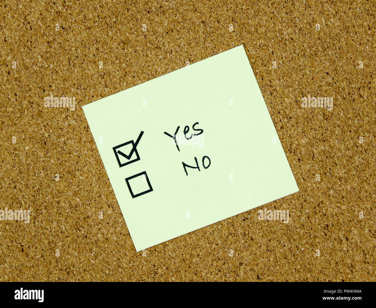 A yellow sticky note with yes / no written on it on a cork board ...