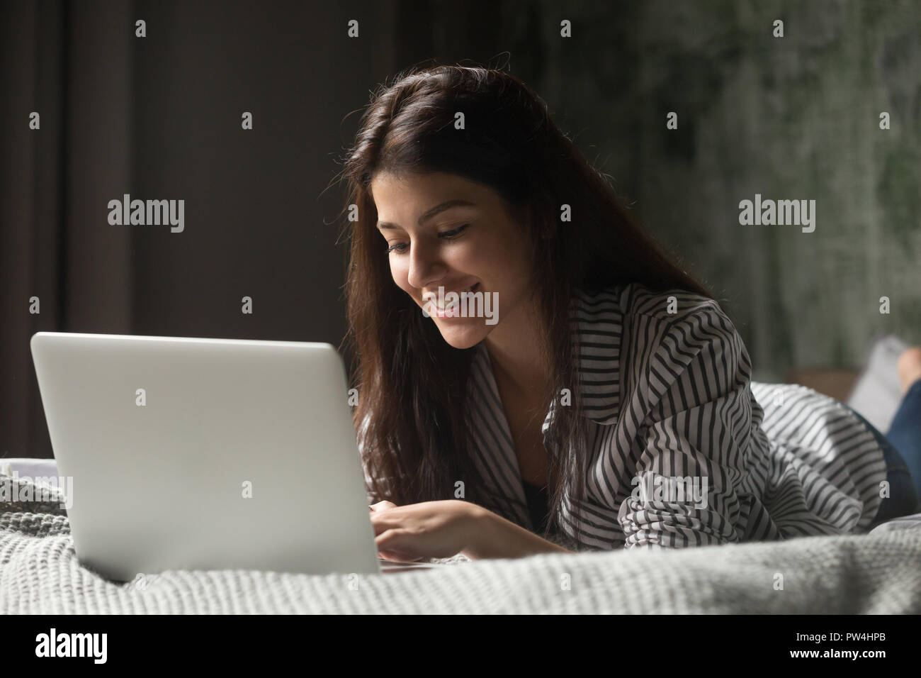 Young positive woman using computer lying on bed at home Stock Photo ...