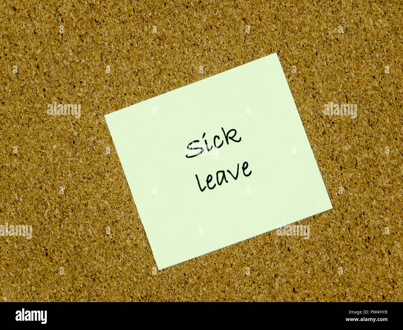 A yellow sticky note with sick leave written on it on a cork board ...