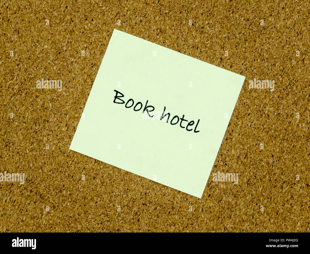 A yellow sticky note with book hotel written on it on a cork board ...