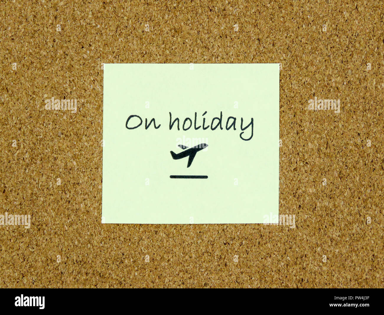 A yellow sticky note with on holiday written on it on a cork board ...