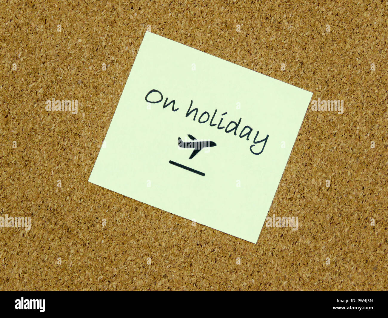 A yellow sticky note with on holiday written on it on a cork board ...
