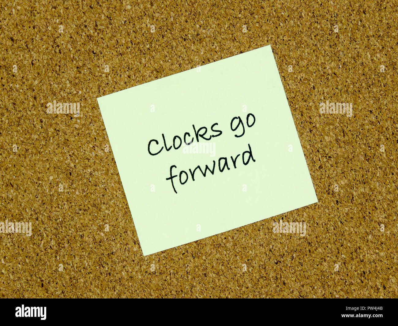 A yellow sticky note with clocks go forward written on it on a cork ...