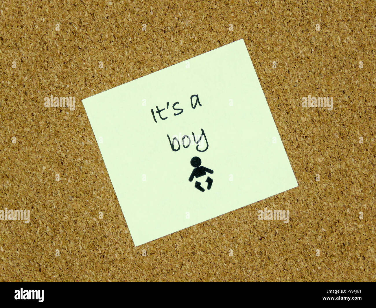 A yellow sticky note with its a boy written on it on a cork board ...
