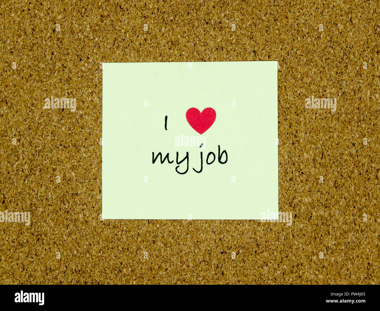 A yellow sticky note with I love my job written on it on a cork board ...