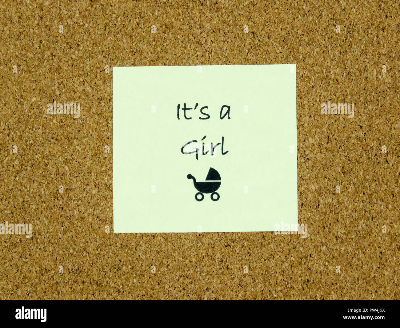 A yellow sticky note with It's a girl written on it on a cork board ...