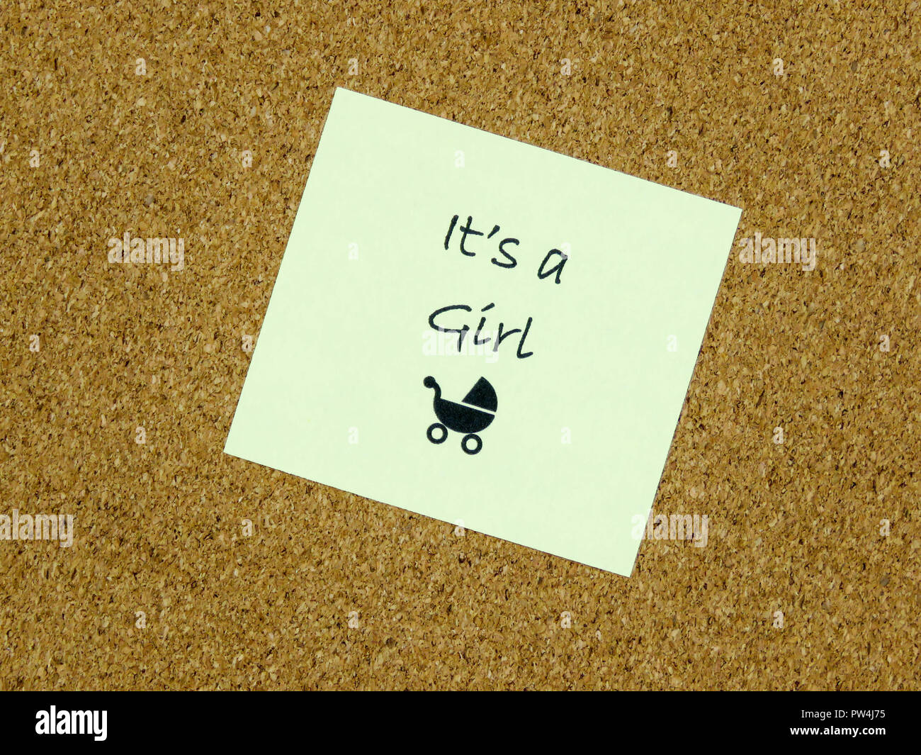 A yellow sticky note with It's a girl written on it on a cork board ...