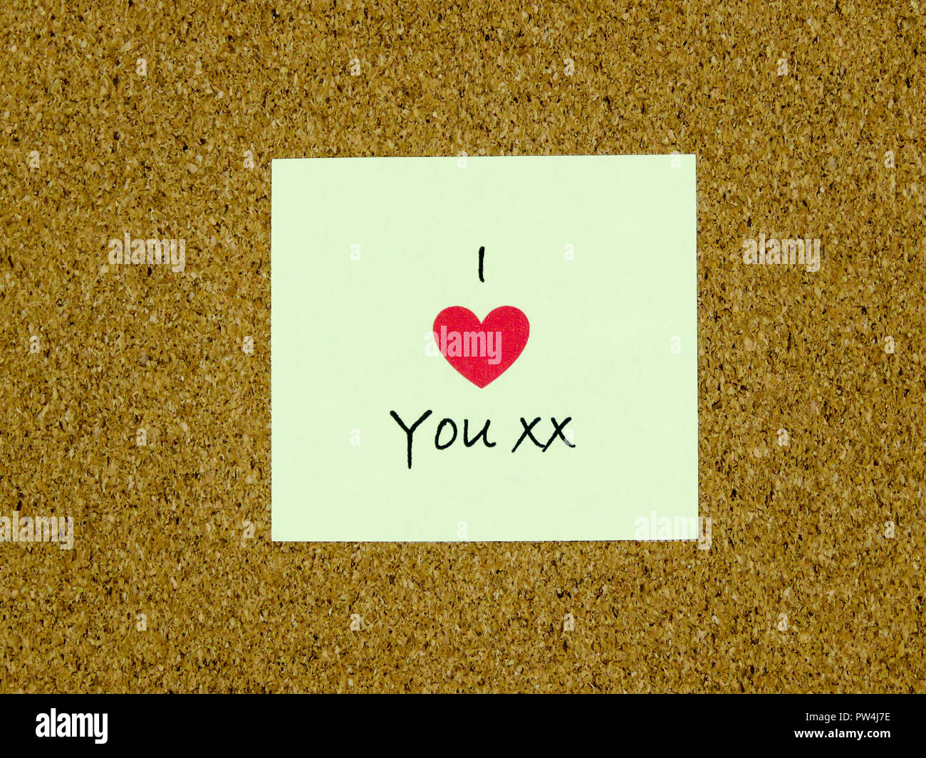 A yellow sticky note with I love you written on it on a cork board ...