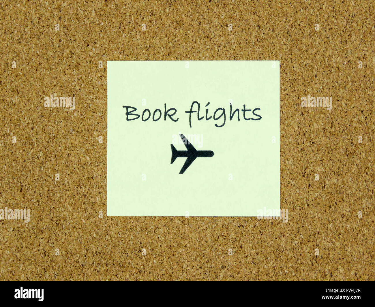 A yellow sticky note with book flights written on it on a cork board ...