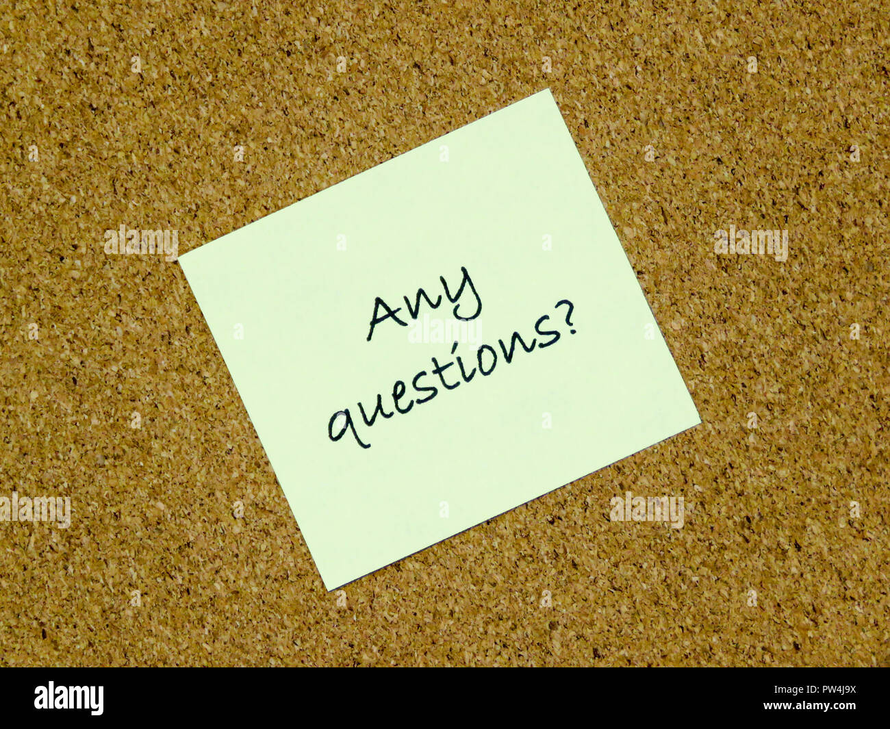 A yellow sticky note with any questions written on it on a cork board ...
