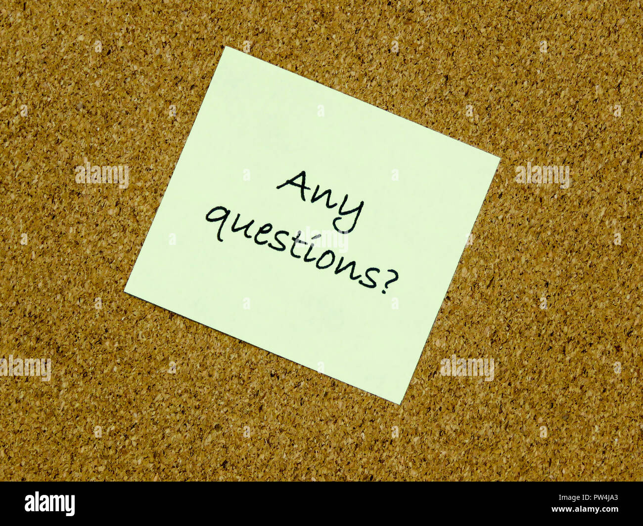A yellow sticky note with any questions written on it on a cork board ...
