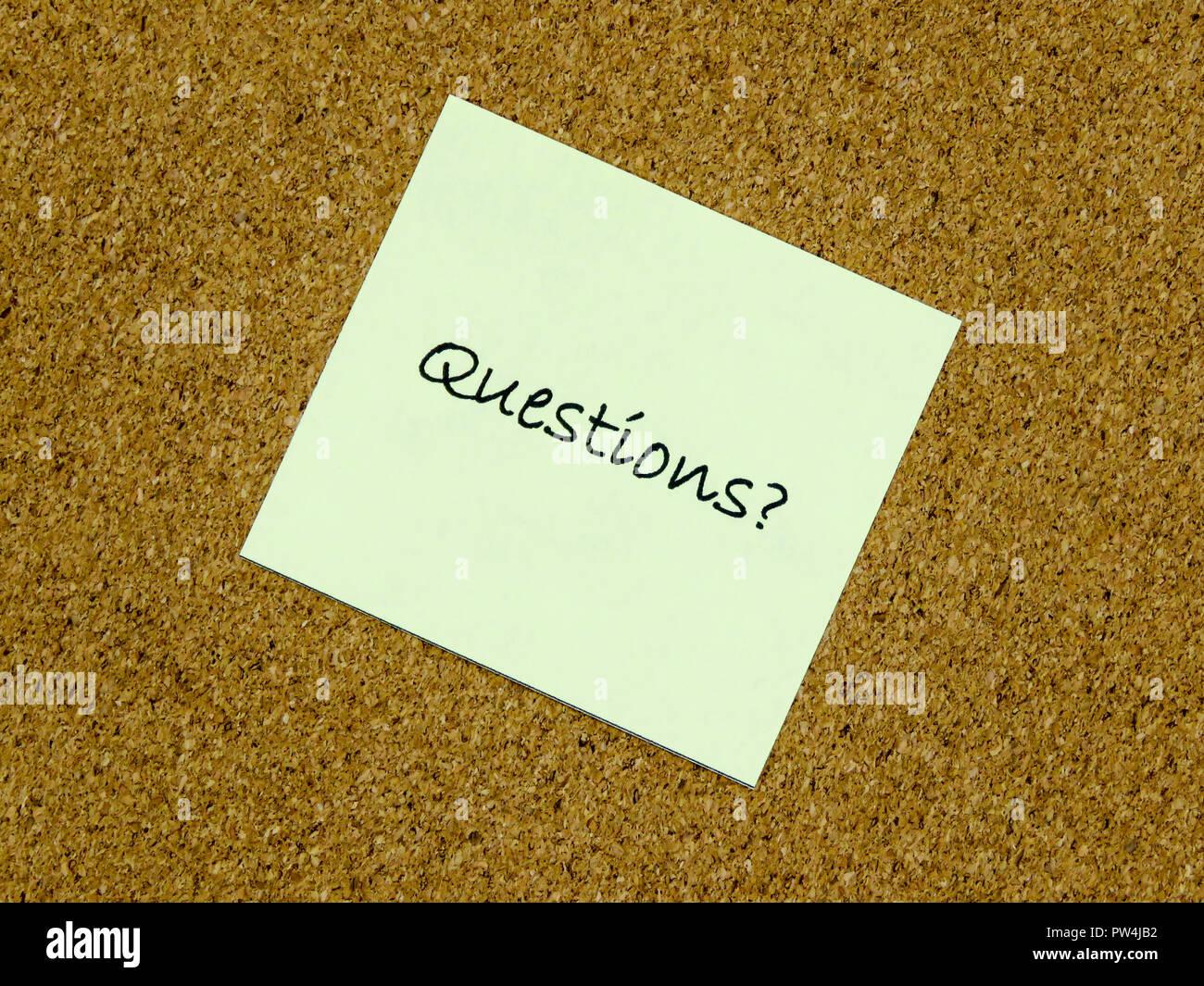 A yellow sticky note with questions written on it on a cork board ...
