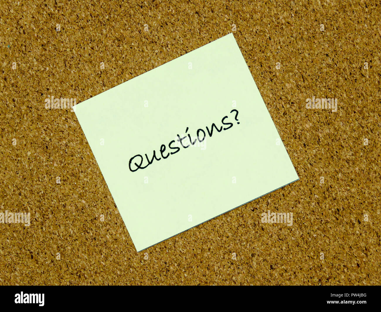 A yellow sticky note with questions written on it on a cork board ...