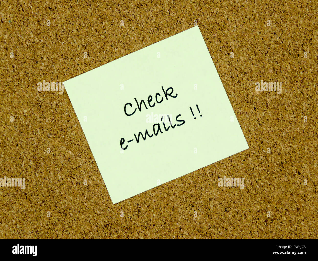 A yellow sticky note with check e-mails written on it on a cork board ...