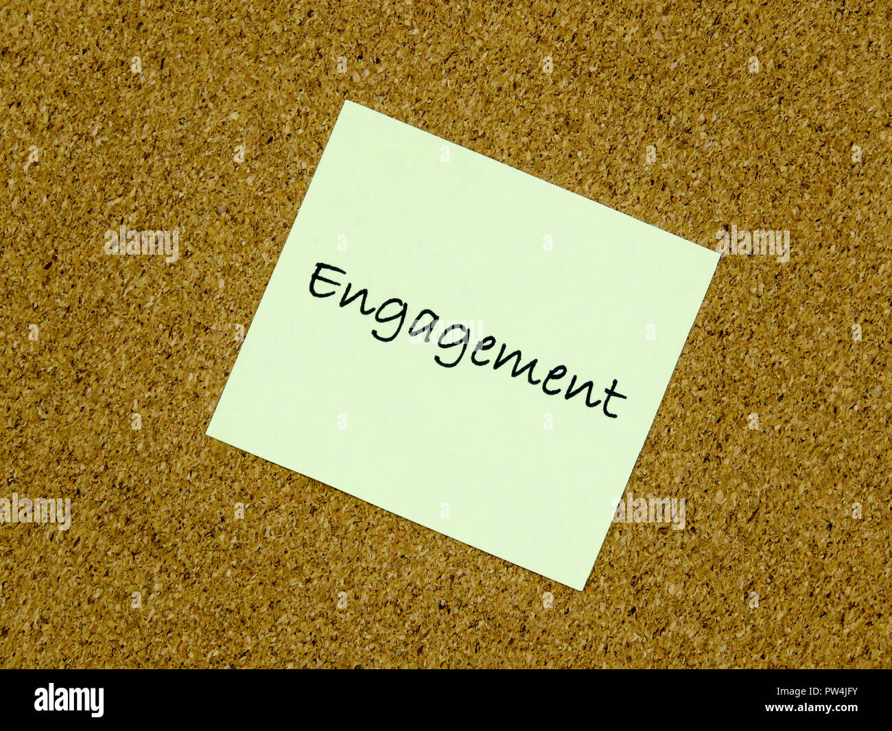 A yellow sticky note with engagement written on it on a cork board ...