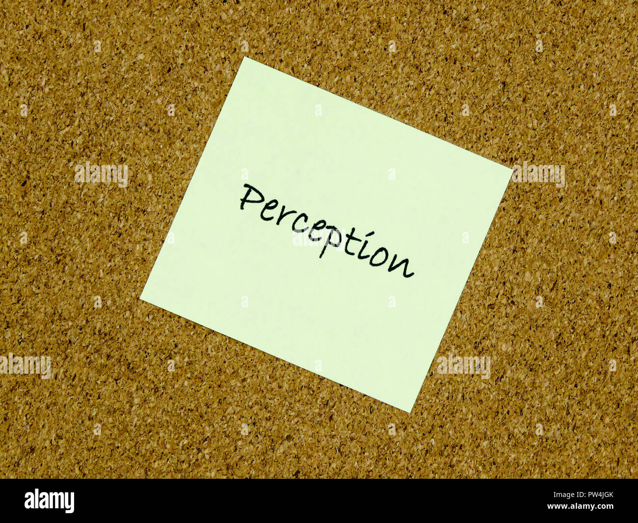 A yellow sticky note with perception written on it on a cork board ...