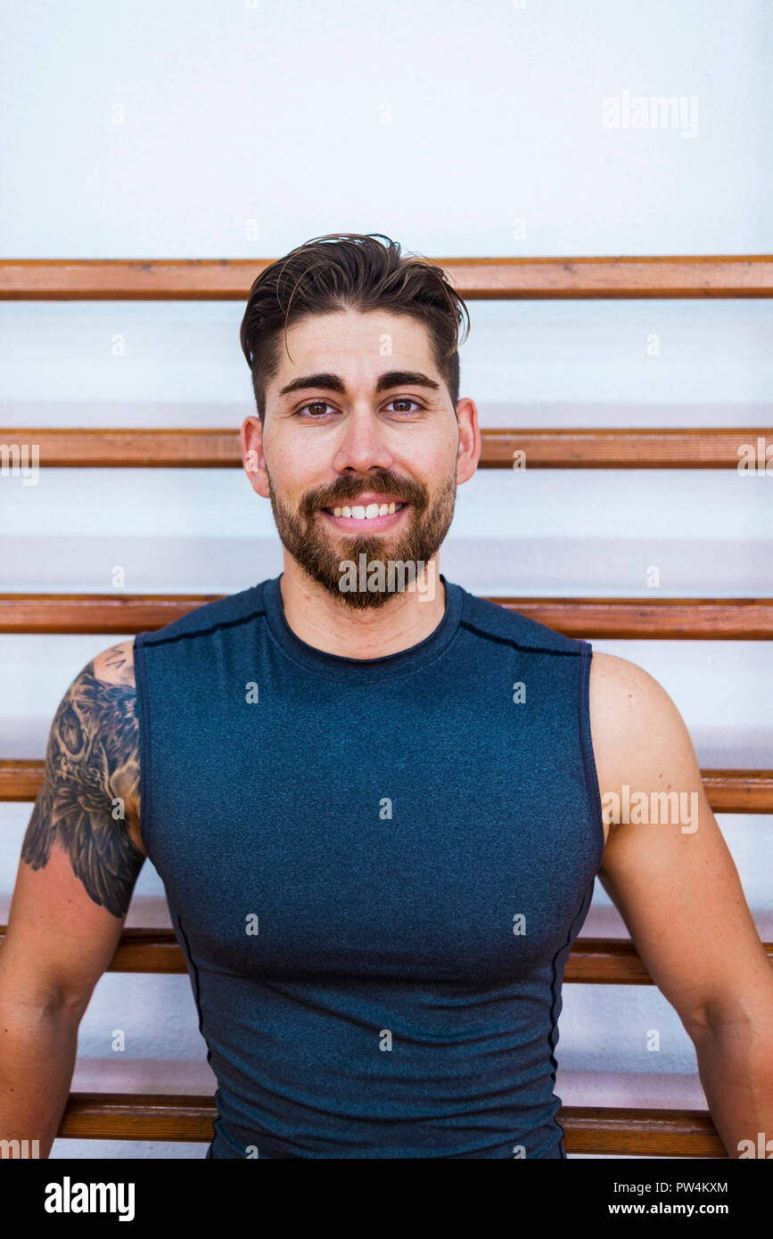 Portrait of confident smiling athlete standing against wall bars in gym ...
