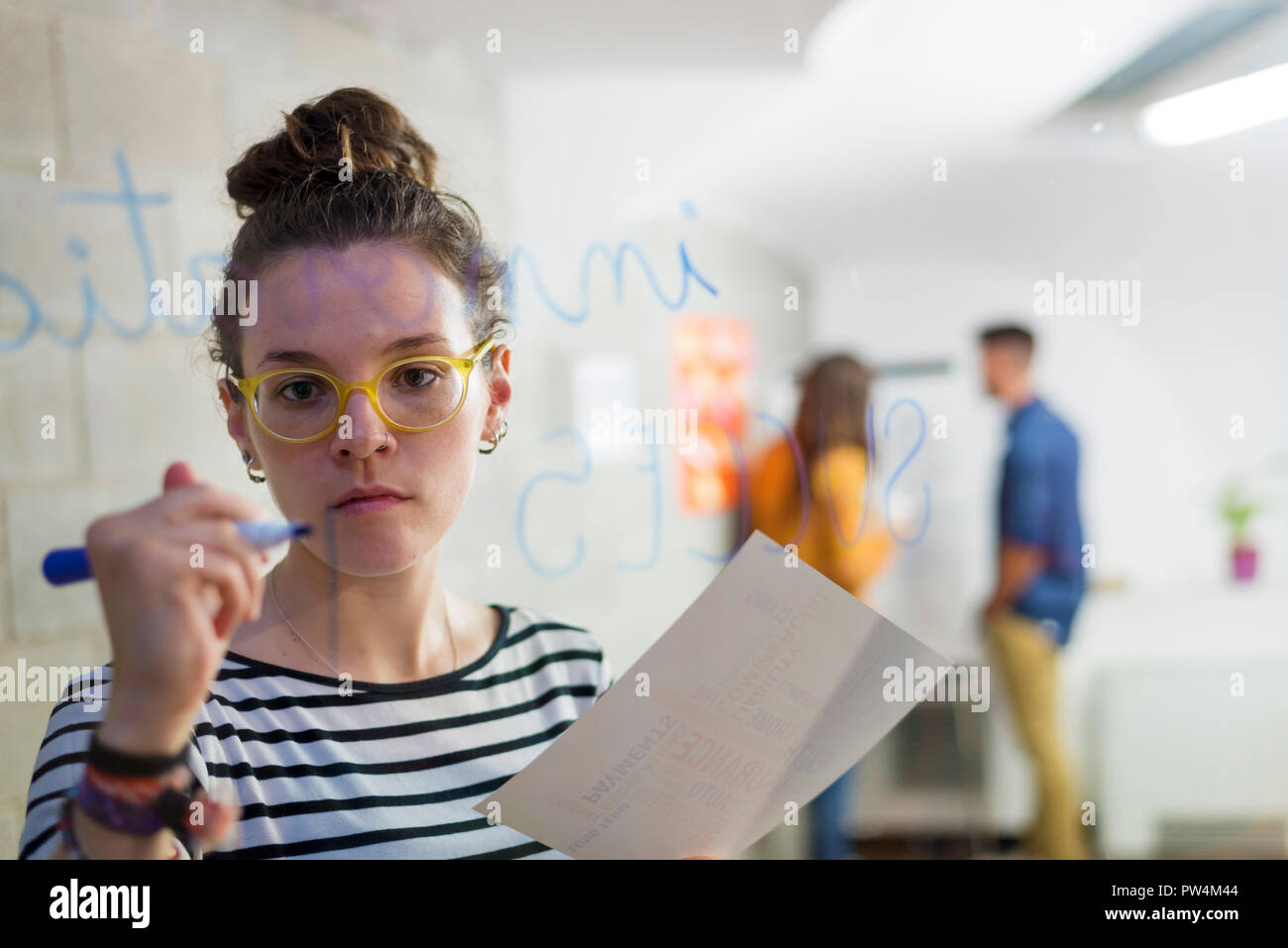 businesswoman writing on window while colleagues discussing in ...