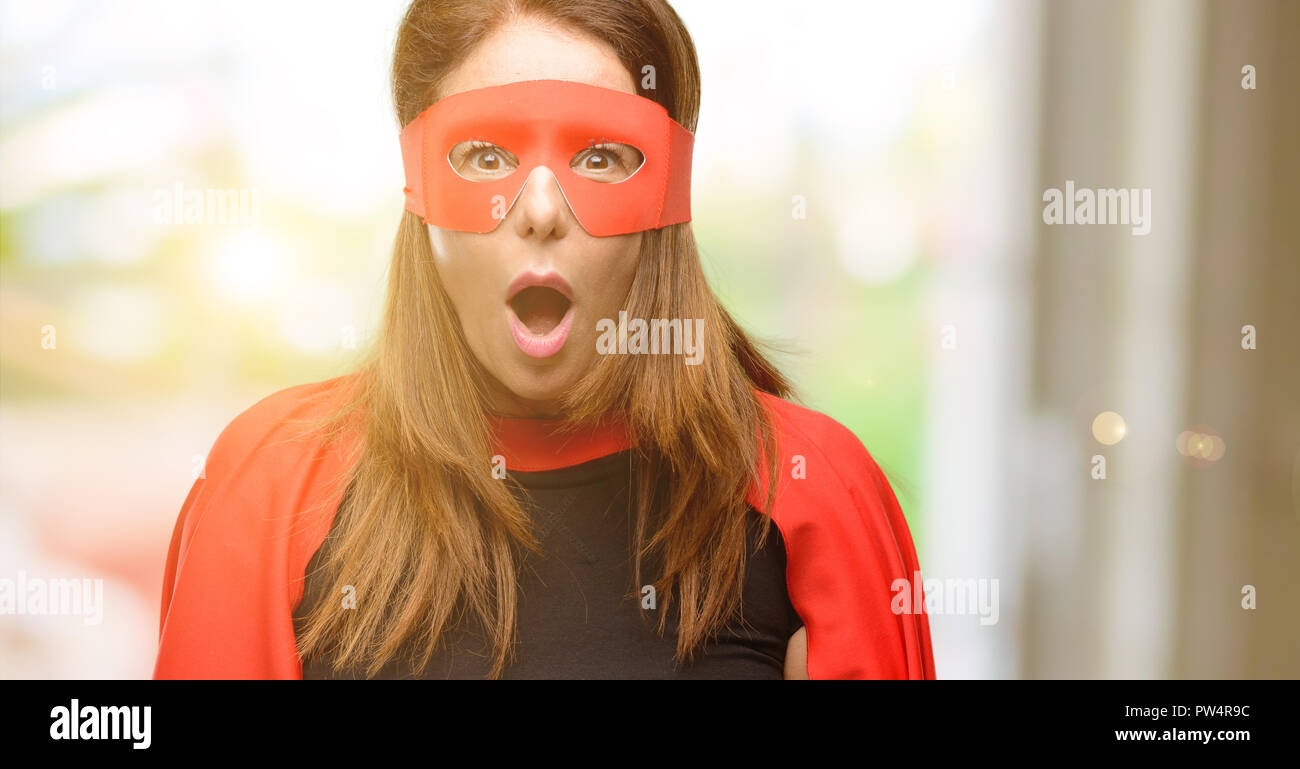 Middle age super hero woman wearing red mask and cape scared in shock ...