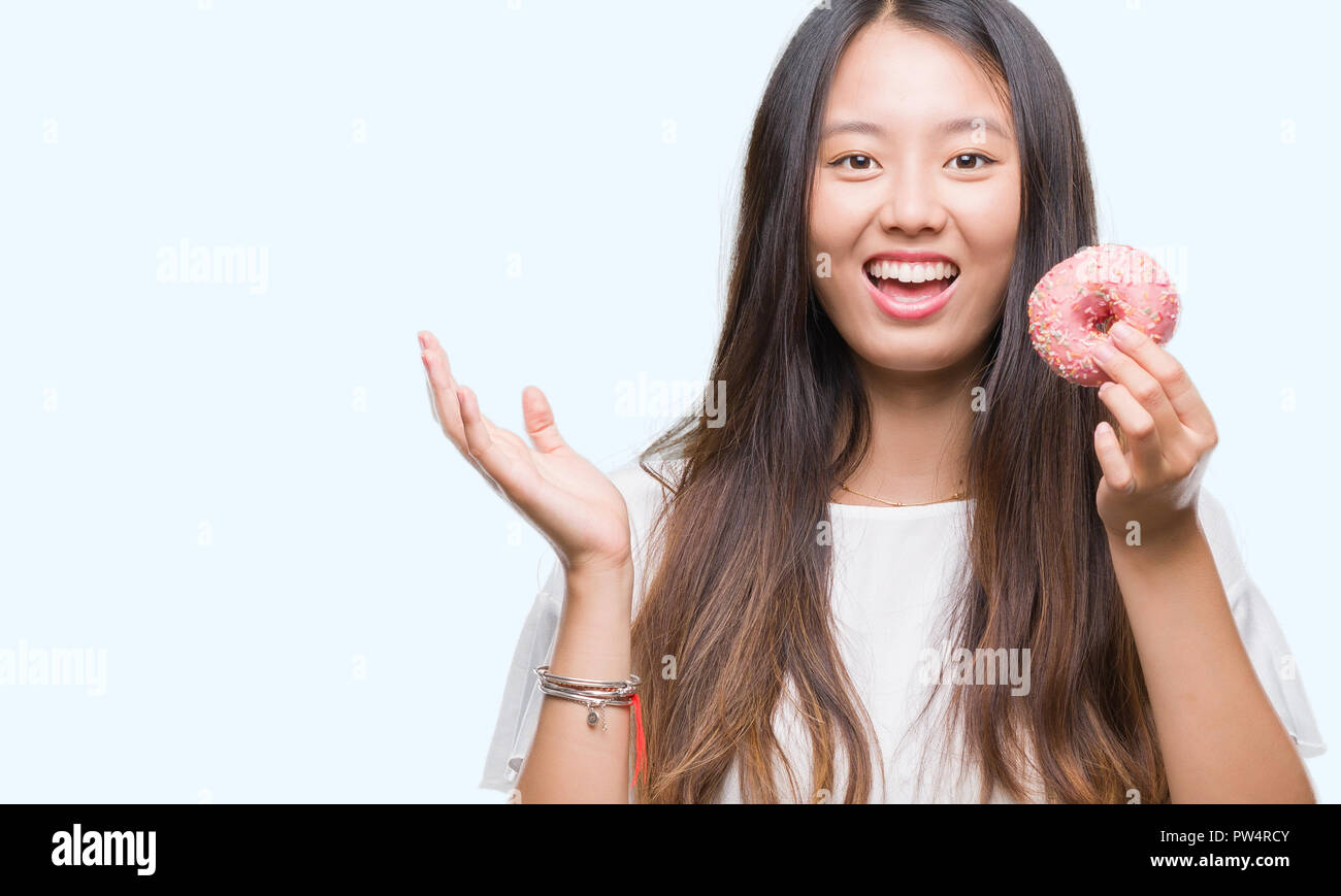 Young asian woman eating donut over isolated background very happy and ...