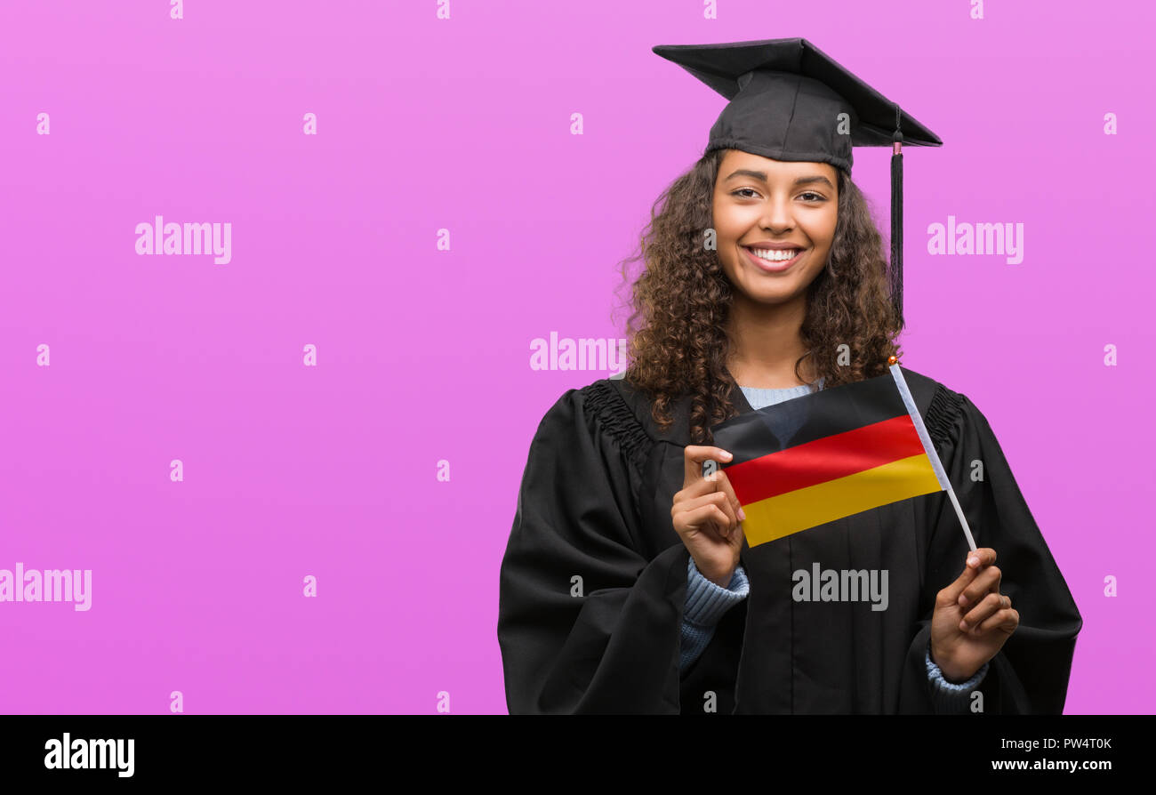 Young hispanic woman wearing graduation uniform holding flag of Germany ...