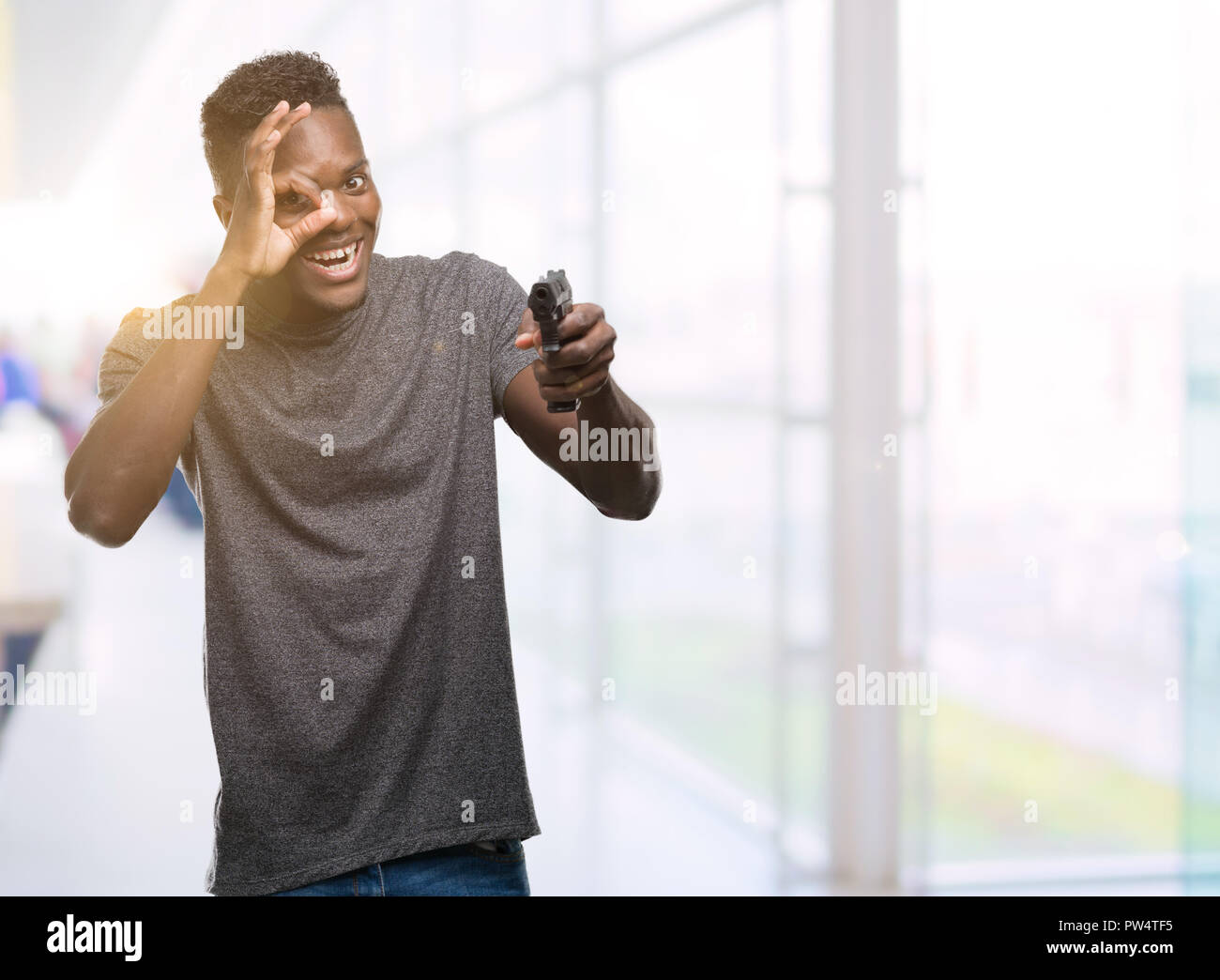 Young african american man holding a gun with happy face smiling doing ...