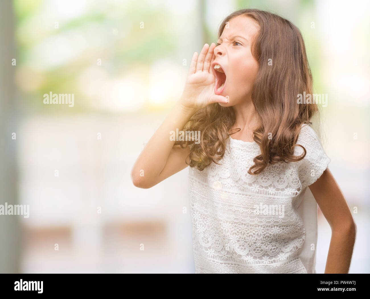 Brunette hispanic girl shouting and screaming loud to side with hand on ...