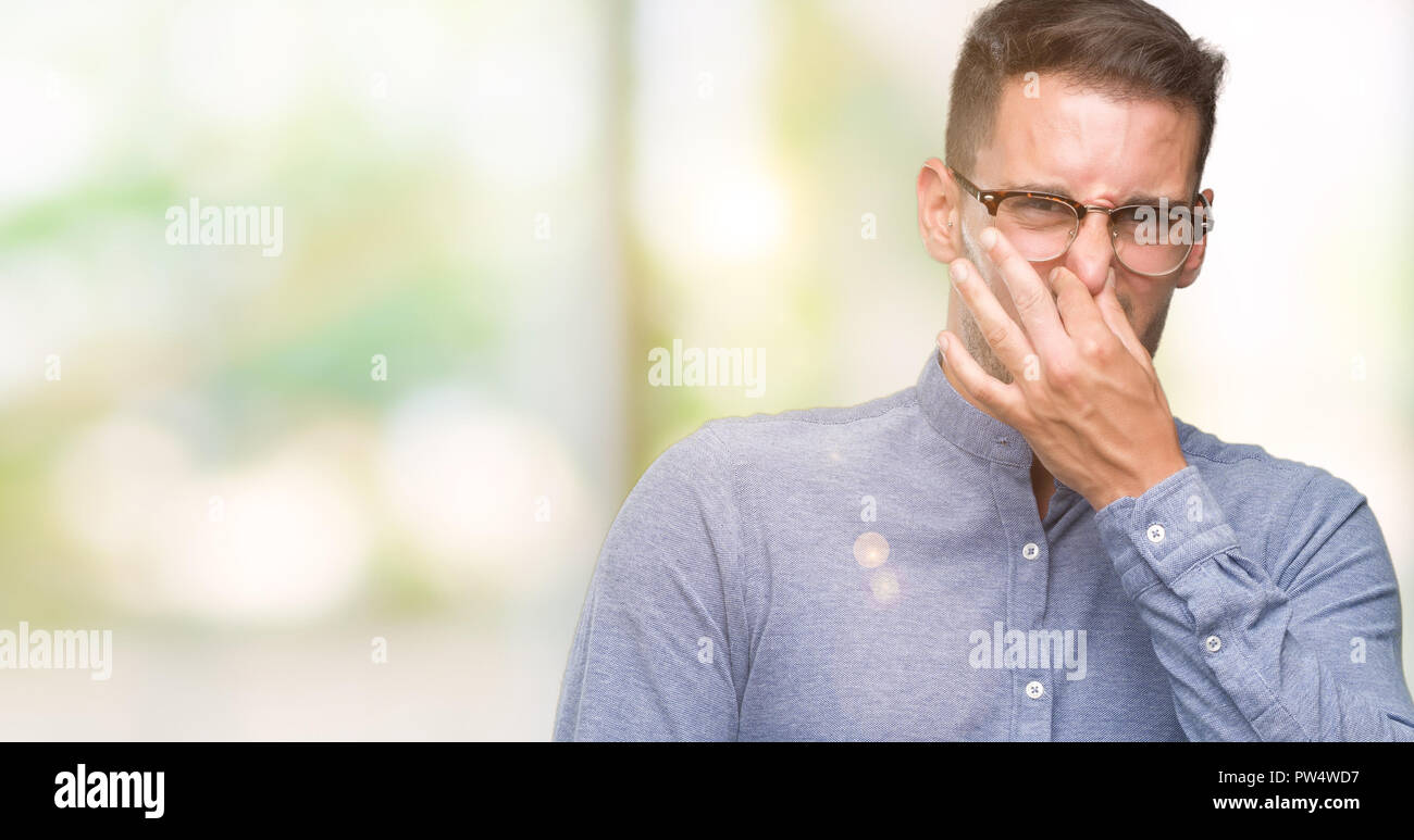 Handsome young elegant man wearing glasses smelling something stinky ...