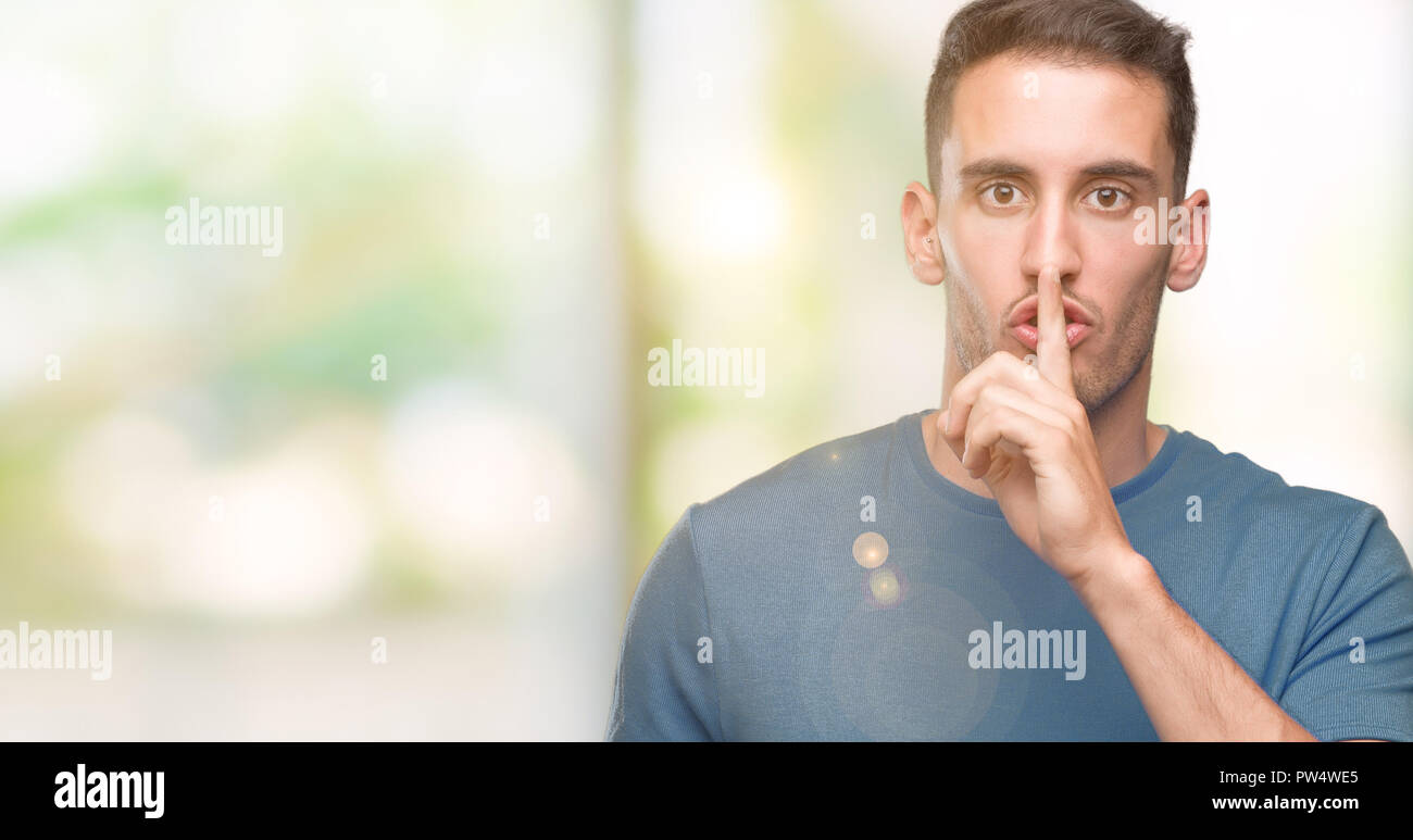 Handsome young casual man asking to be quiet with finger on lips ...