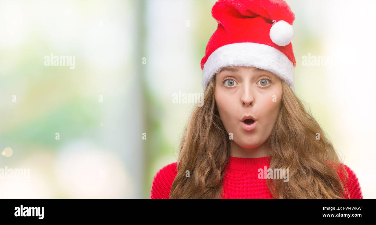 Young blonde woman wearing santa claus hat scared in shock with a ...